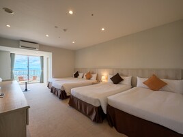Quarto de hotel com três camas, uma escrivaninha e varanda com vista.