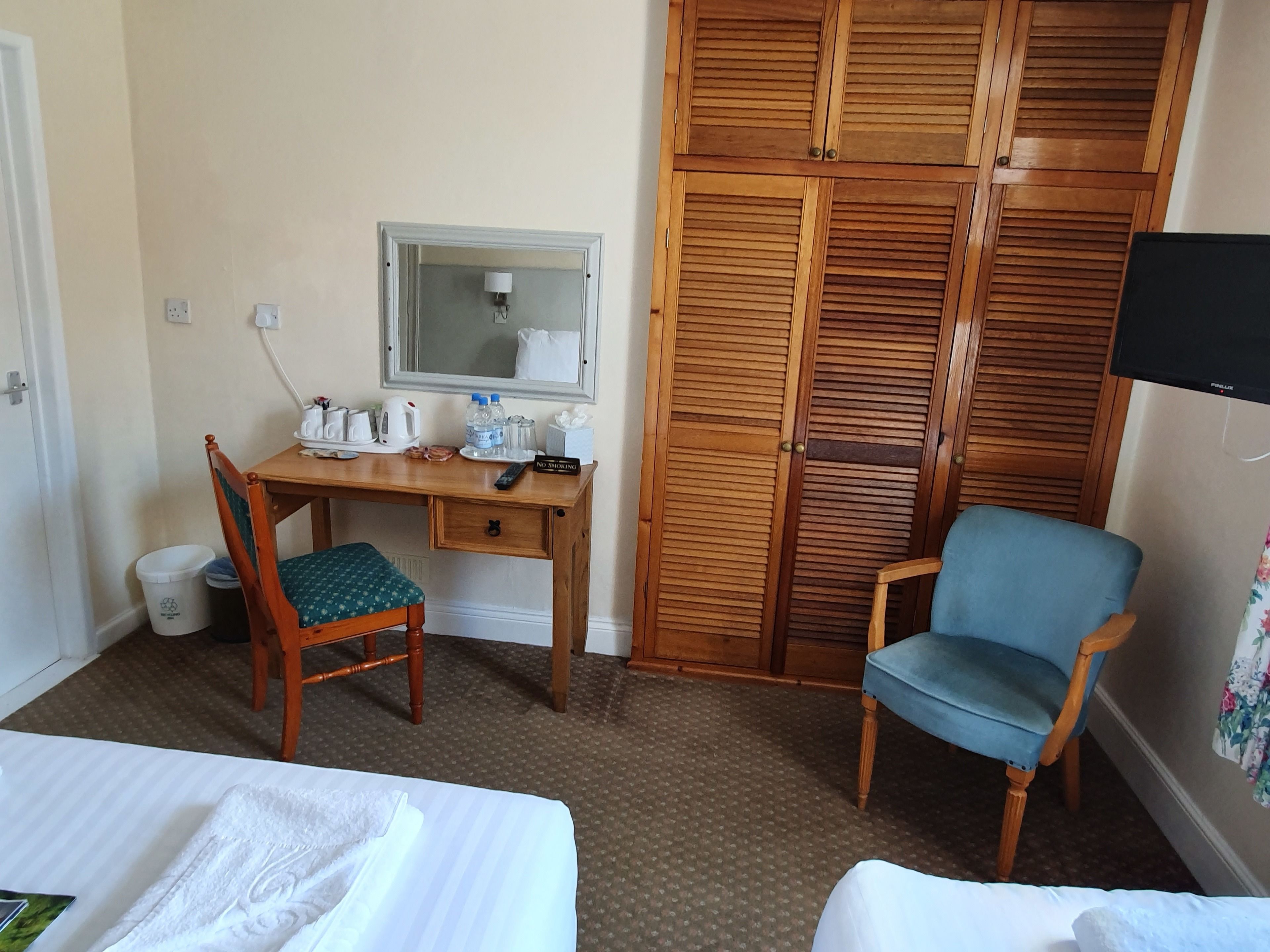 Quarto de hotel com escrivaninha de madeira, cadeira, cama e guarda-roupa.