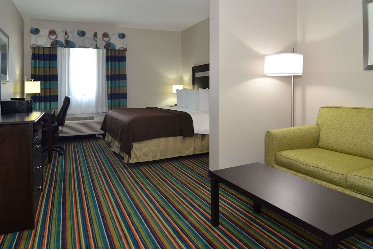 Quarto de hotel com cama, escrivaninha, poltrona, sofá e abajur.