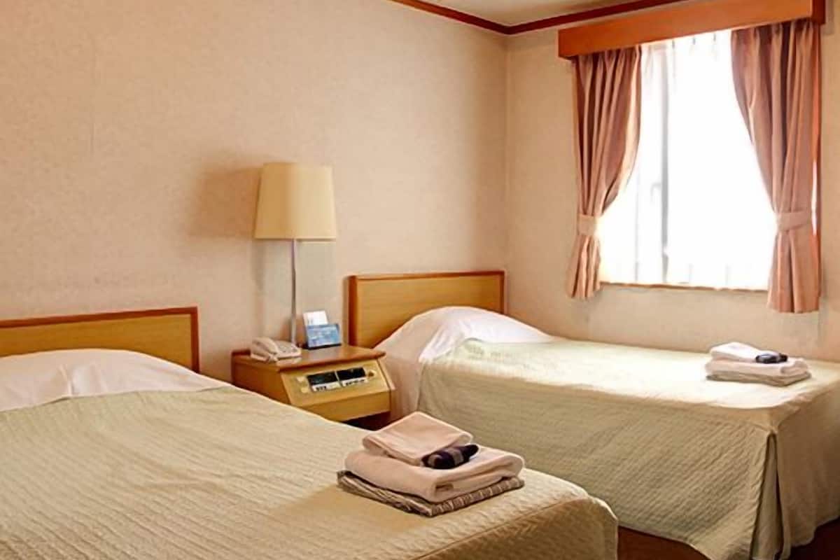Quarto de hotel com duas camas, uma mesa de cabeceira com abajur e uma janela com cortinas.