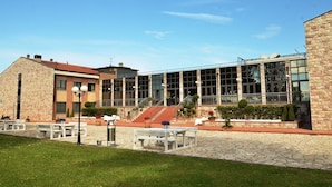 Um edifício com fachada de pedra, grandes janelas e um pátio pavimentado com área para sentar ao ar livre.