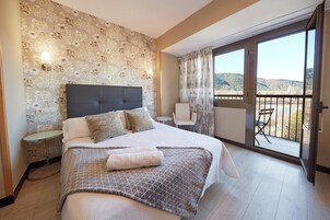 Quarto de hotel com cama grande, uma mesinha, uma cadeira e varanda com vista para as colinas.