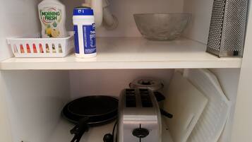 Uma prateleira na cozinha com um frasco de detergente, um recipiente de bicarbonato de sódio, um ralador e uma frigideira.