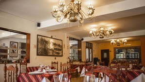 Restaurante com várias mesas de jantar preparadas para os hóspedes, com um candelabro e um quadro grande na parede.