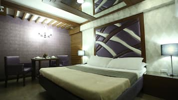 Quarto de hotel com uma cama grande, uma escrivaninha com cadeira, uma mesinha com um vaso e uma mesa de cabeceira com abajur.