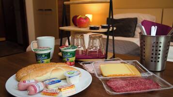 Uma mesa de café da manhã com um prato de comida, uma xícara de iogurte, uma garrafa de suco, um sanduíche e um recipiente com carne.