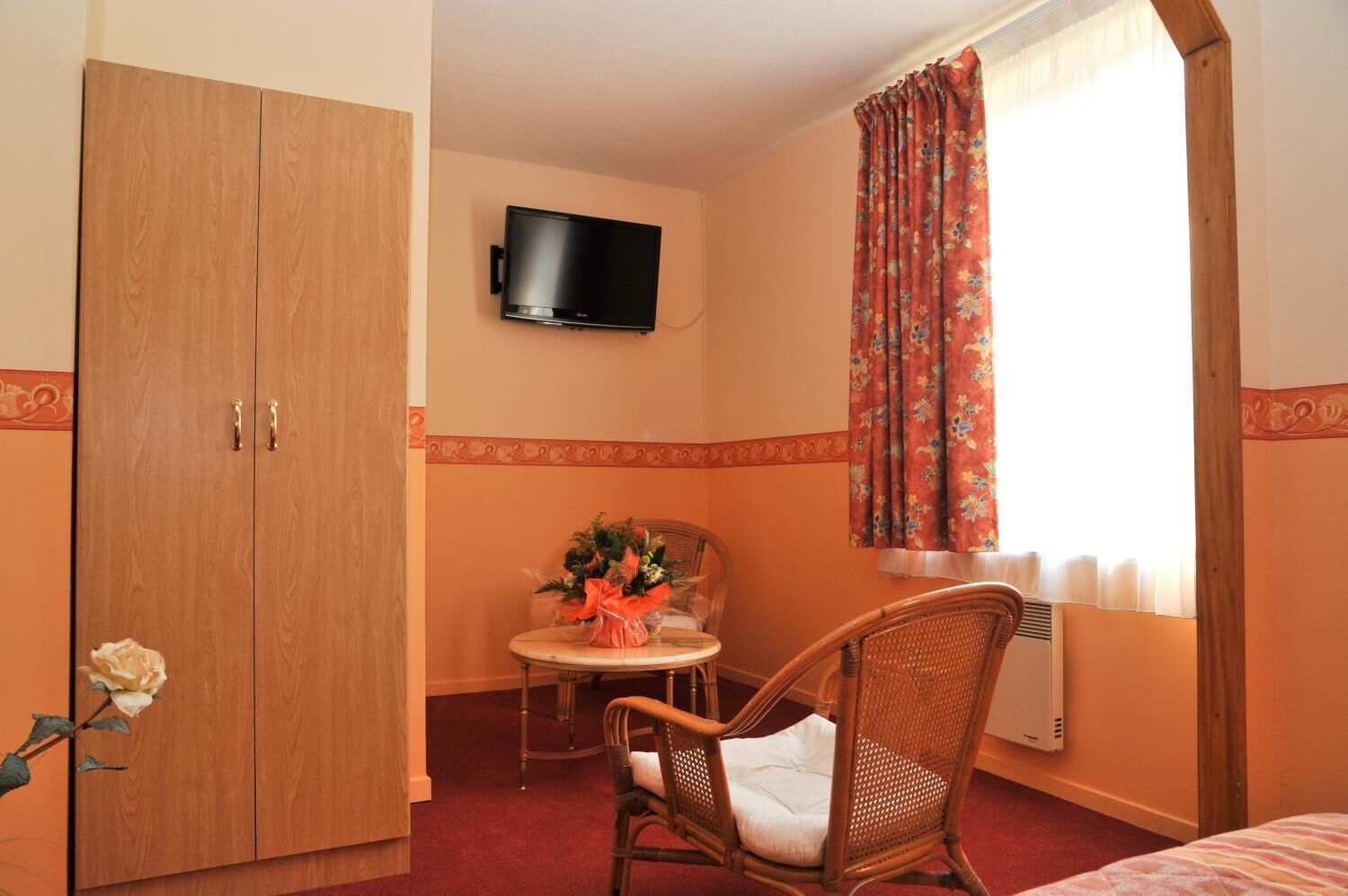 Quarto com guarda-roupa de madeira, televisão na parede, mesa de jantar com cadeiras e janela com cortinas.