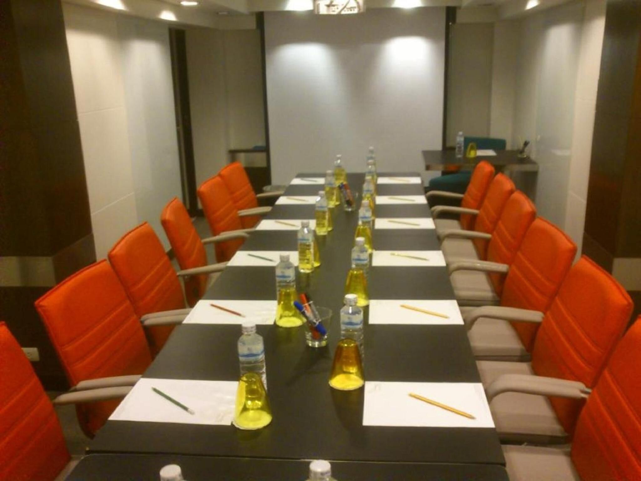 Uma sala de conferências com uma mesa comprida, cadeiras laranja e garrafas de água sobre a mesa.