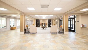 Um hall amplo com uma mesa central, duas poltronas e um balcão de recepção.