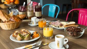 Mesa de café da manhã com croissants, frutas, suco, café e chocolate.