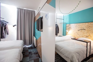 Quarto de hotel com duas camas, televisão, cabeceira de madeira e janela com cortinas.