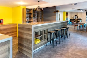 Uma área de bar moderna com balcão de madeira, banquetas e luminárias pendentes.
