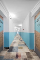 Um corredor de hotel comprido e estreito, com paredes azuis e brancas, um carpete estampado e portas com números de quartos.