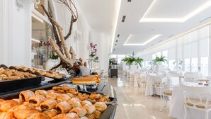 Uma área de buffet com diversos doces e uma sala de estar com mesas e cadeiras brancas.