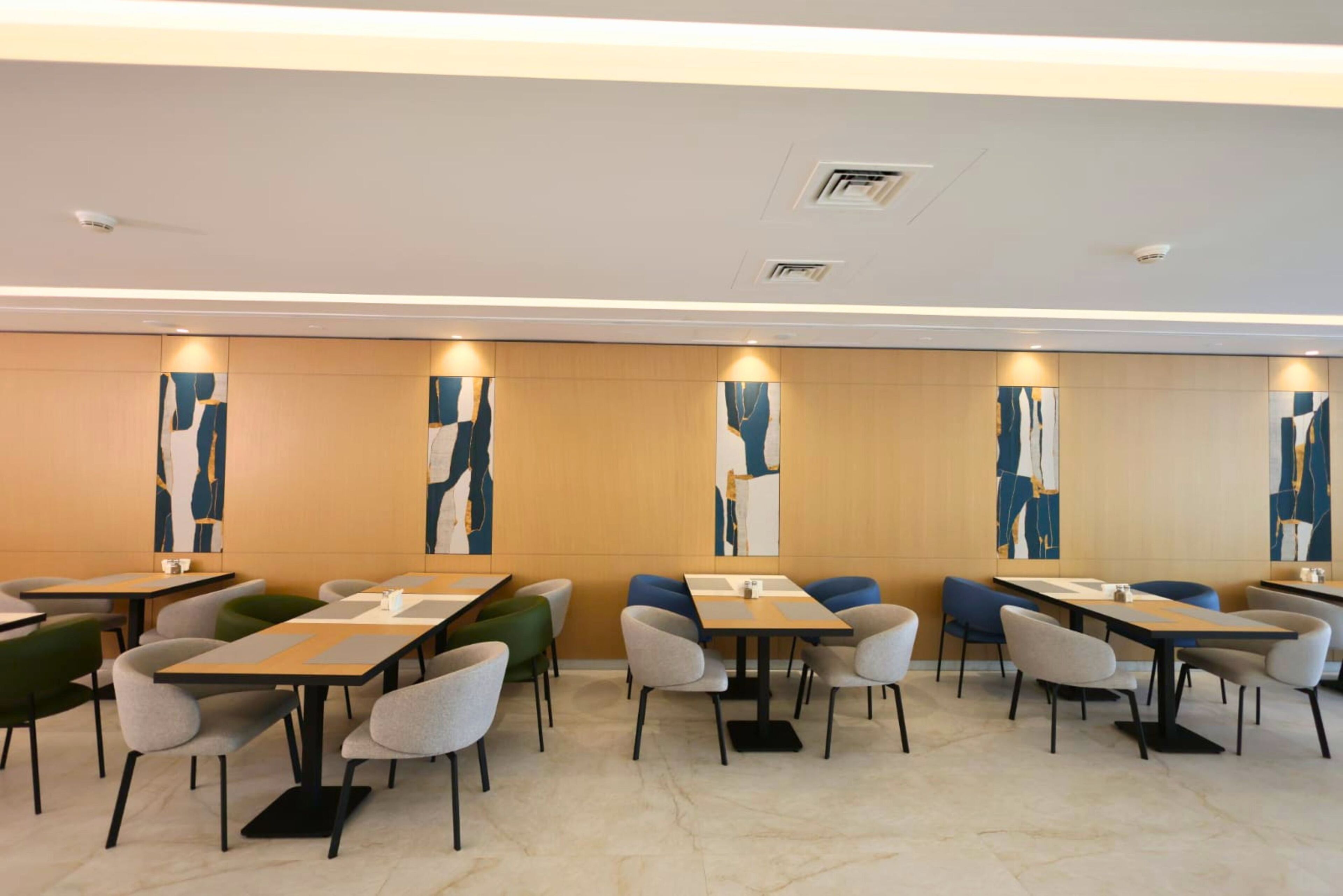 Um lobby de hotel moderno, com design clean, com várias áreas de estar com mesas e cadeiras, e arte abstrata nas paredes.