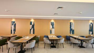 Um lobby de hotel moderno, com design clean, com várias áreas de estar com mesas e cadeiras, e arte abstrata nas paredes.