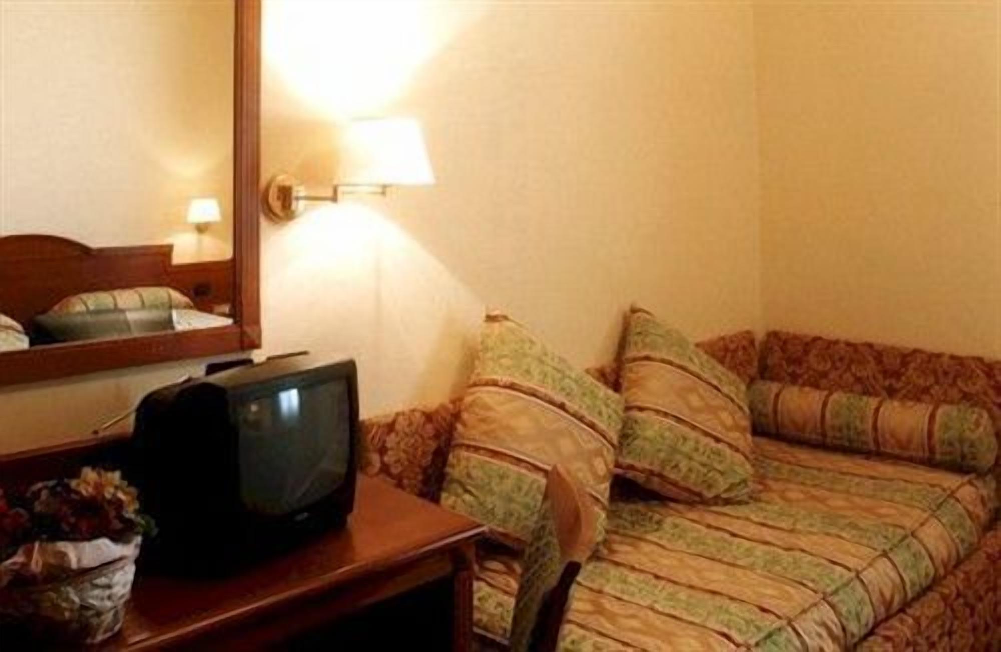 Quarto de hotel com uma cama, televisão sobre uma mesa de madeira e um abajur.