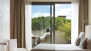 Quarto de hotel com uma banheira grande, varanda com vista para áreas verdes e cama com almofadas.