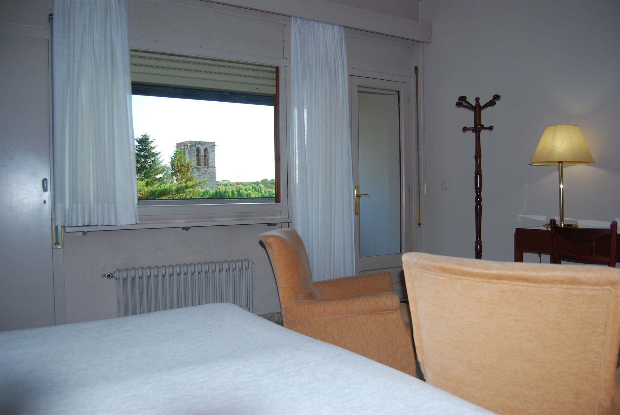 Quarto de hotel com uma cama, uma cadeira, um abajur e vista para uma torre pela janela.