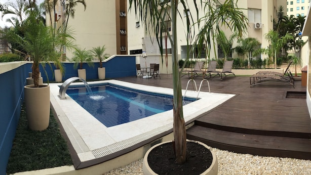 Piscina com cascata, rodeada por um deck com assentos e plantas em vasos.