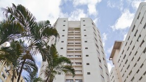Um edifício com vários andares e entrada central, rodeado por vegetação e palmeiras.