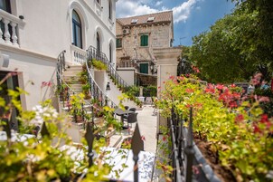 Um pátio com uma escadaria que leva a uma varanda, rodeado por plantas em vasos e móveis de jardim.