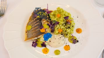 Um prato branco com peixe, risoto verde e diversos acompanhamentos.