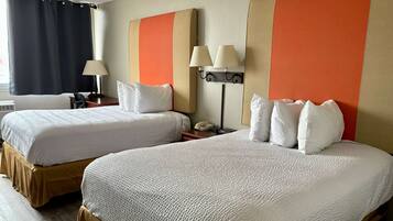 Quarto de hotel com duas camas, uma escrivaninha, um abajur e um telefone.