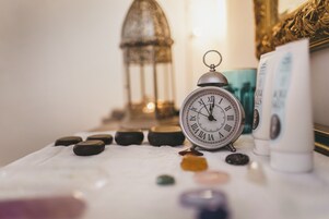 Uma mesa com um despertador, uma vela e um frasco de loção.