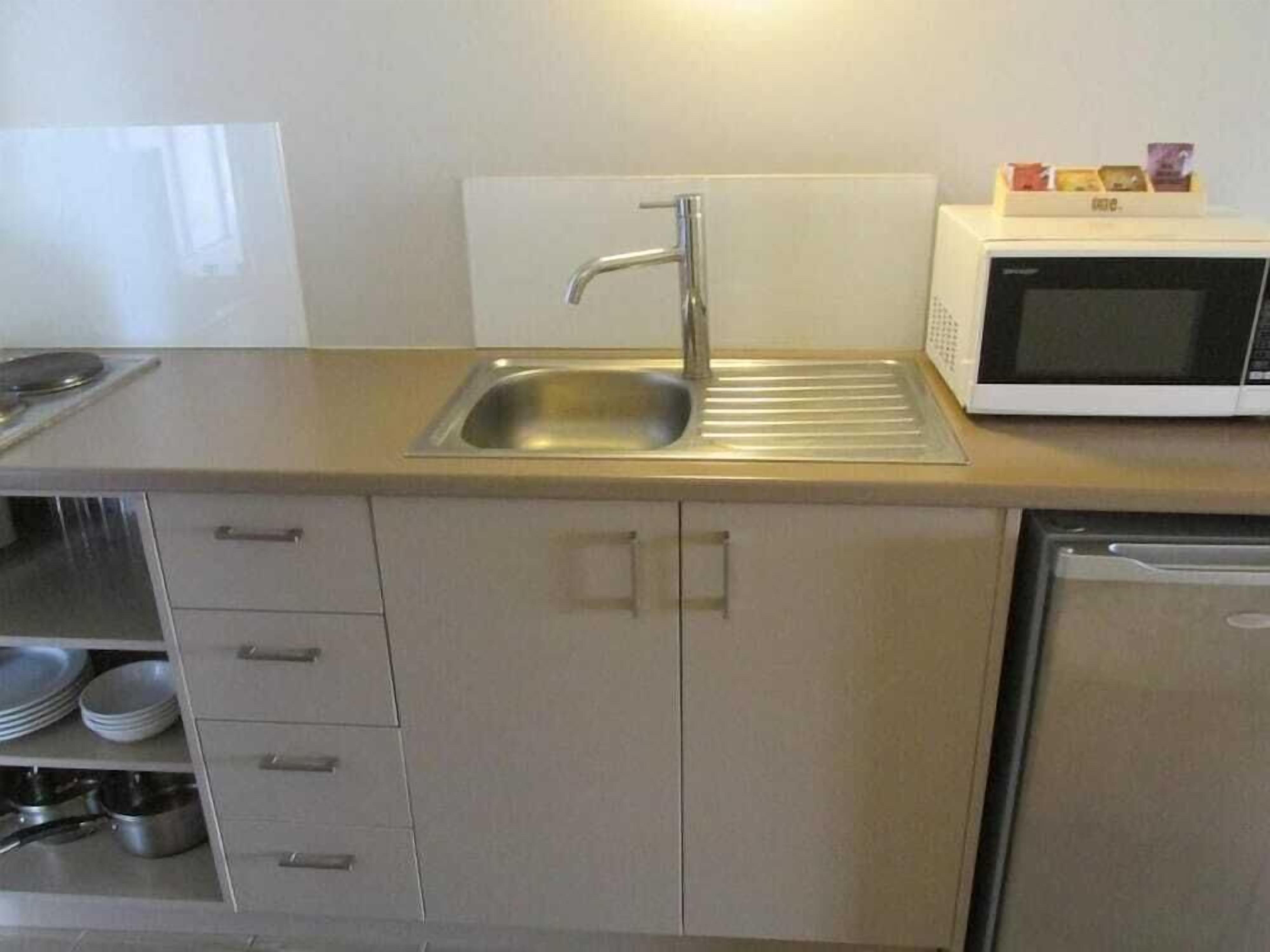 Cozinha com pia de aço inoxidável, micro-ondas e armários.