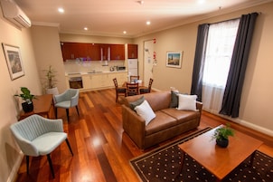 Uma sala de estar moderna com um sofá marrom, duas poltronas, uma mesa de jantar e uma cozinha ao fundo.