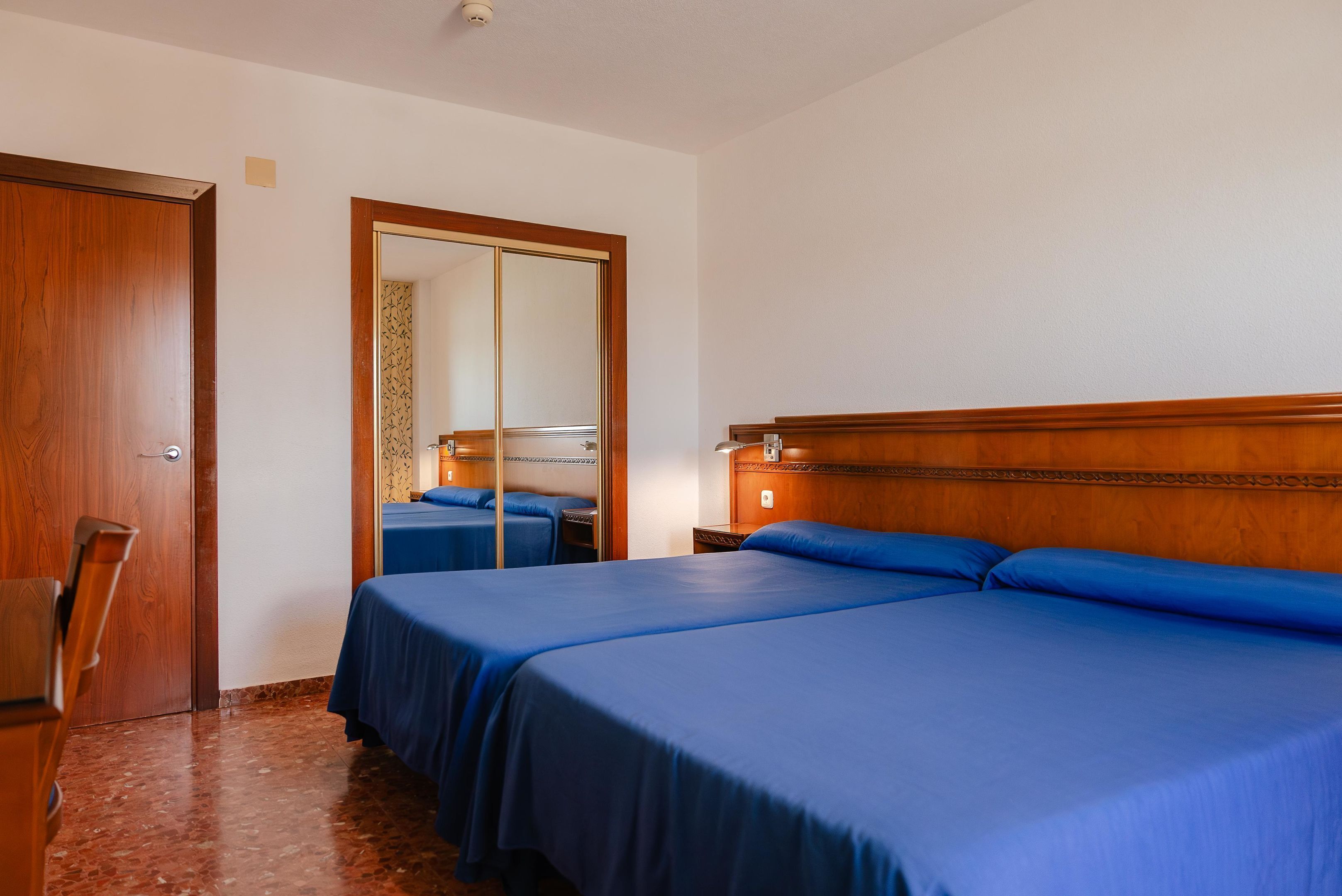 Quarto de hotel com duas camas, cabeceira de madeira, espelho e uma porta.
