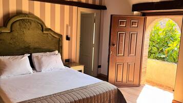 Quarto com cama grande, cabeceira de madeira e vista para um jardim através de uma porta aberta.