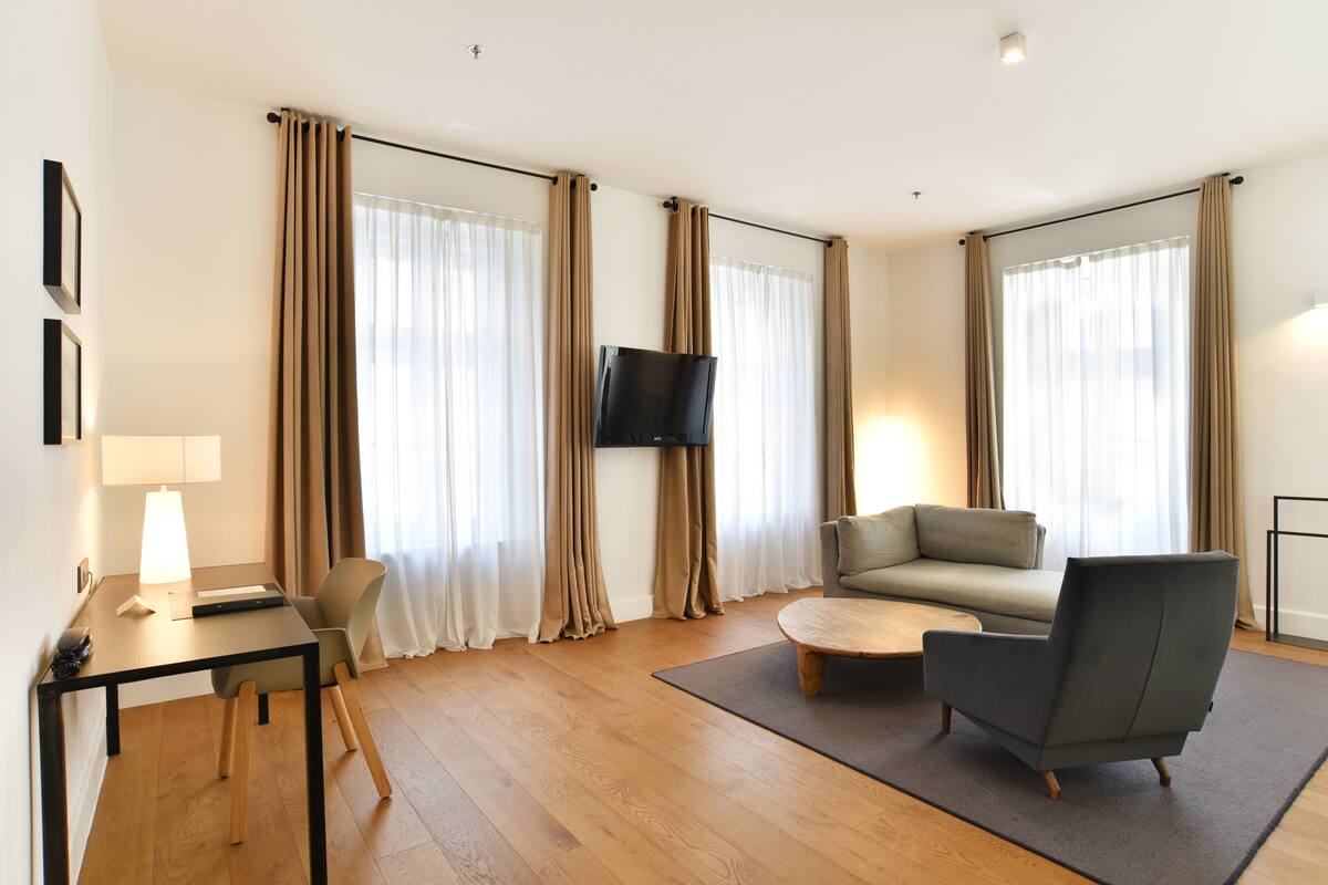 Uma sala de estar moderna com sofá, poltrona, mesa de centro e uma TV na parede.