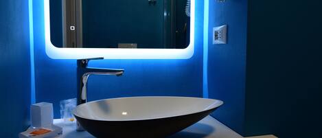 Uma casa de banho moderna com uma grande lavatório suspensa, um espelho iluminado e uma parede azul.