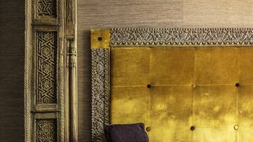 Quarto com sofá estofado em dourado, uma pequena mesa lateral de madeira e detalhes entalhados nas paredes.