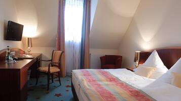 Quarto de hotel com cama, escrivaninha, cadeira, televisão e cortinas.