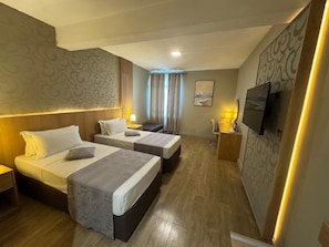 Quarto de hotel com duas camas, uma escrivaninha, uma televisão e um quadro na parede.
