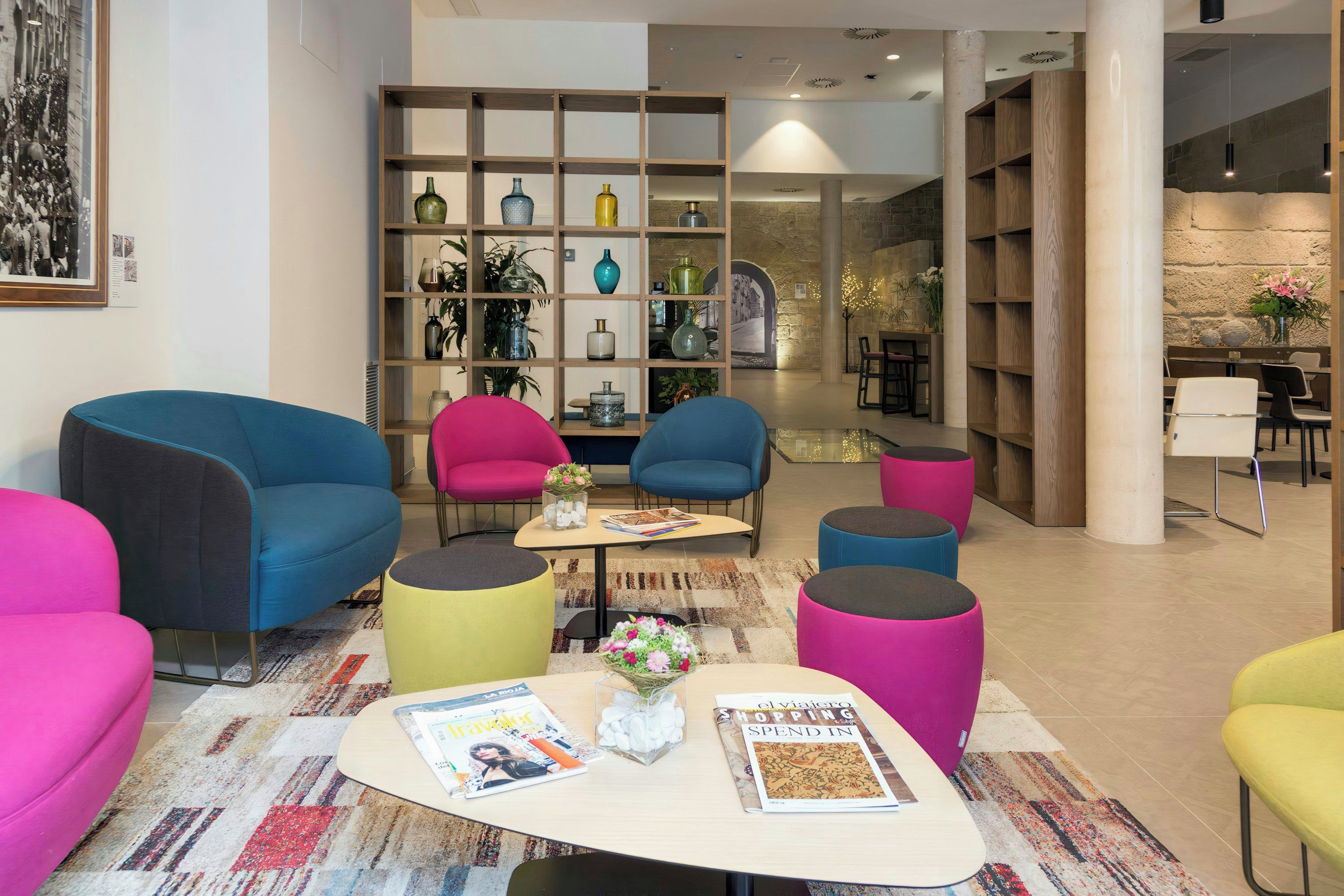 Decoração moderna com assentos coloridos, uma mesa de centro e uma estante repleta de objetos decorativos.