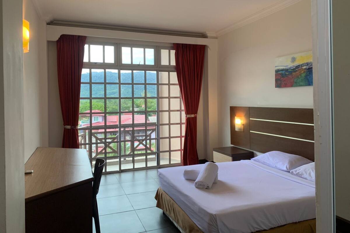 Quarto de hotel com cama, escrivaninha e vista para o oceano através de uma grande janela.