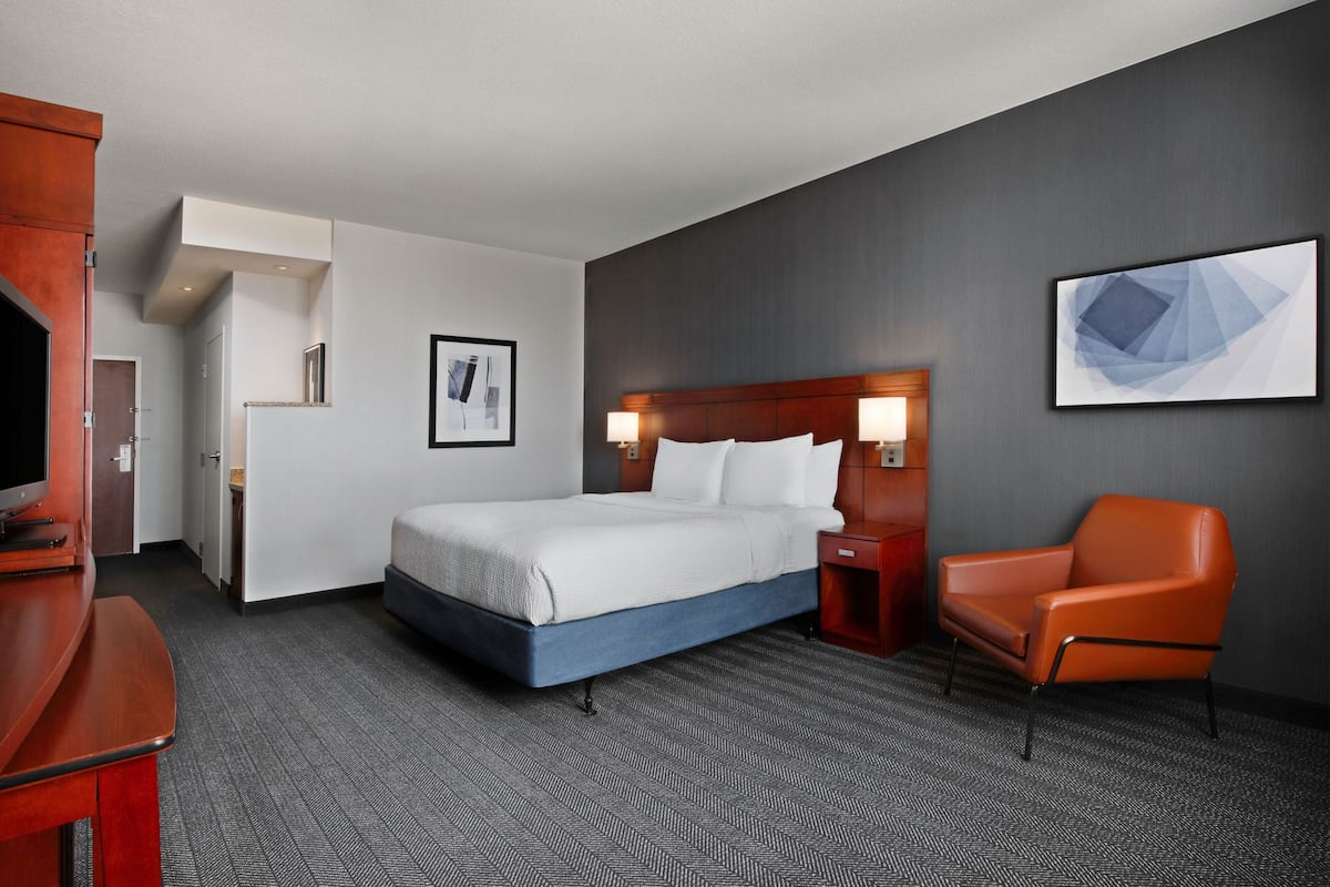 Quarto de hotel com cama, uma cadeira, televisão e obras de arte nas paredes.