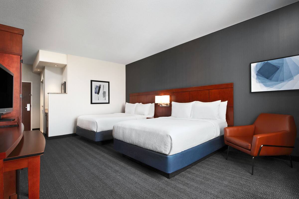 Quarto de hotel com duas camas, uma mesa, uma cadeira e uma televisão.