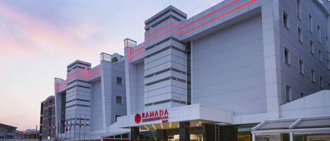 Um hotel moderno com uma placa visível, vários andares e área de estacionamento.