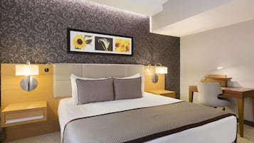 Quarto de hotel com uma cama grande, duas mesas de cabeceira com abajures, uma escrivaninha de madeira e uma cadeira.
