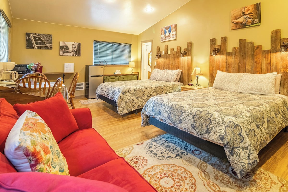 Quarto com duas camas, um sofá vermelho e cabeceira de madeira.
