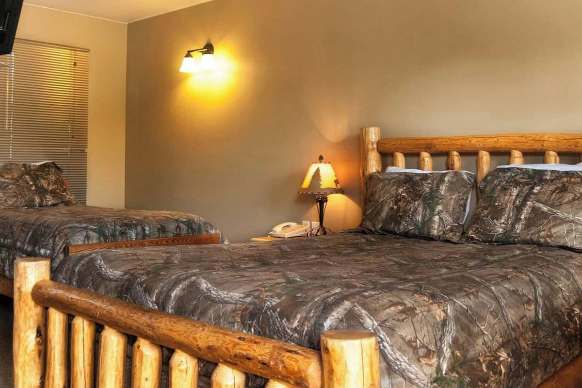 Quarto com duas camas, uma mesa de cabeceira, uma luminária e um ponto de luz na parede.
