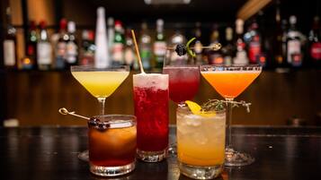 Balcão de bar com cinco coquetéis diferentes, cada um com um detalhe decorativo único.
