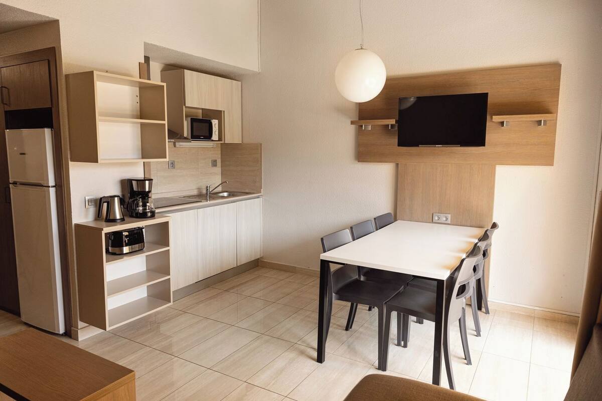 Cozinha moderna com área de refeições, incluindo geladeira, micro-ondas, cafeteira e uma TV de tela plana presa acima do balcão.