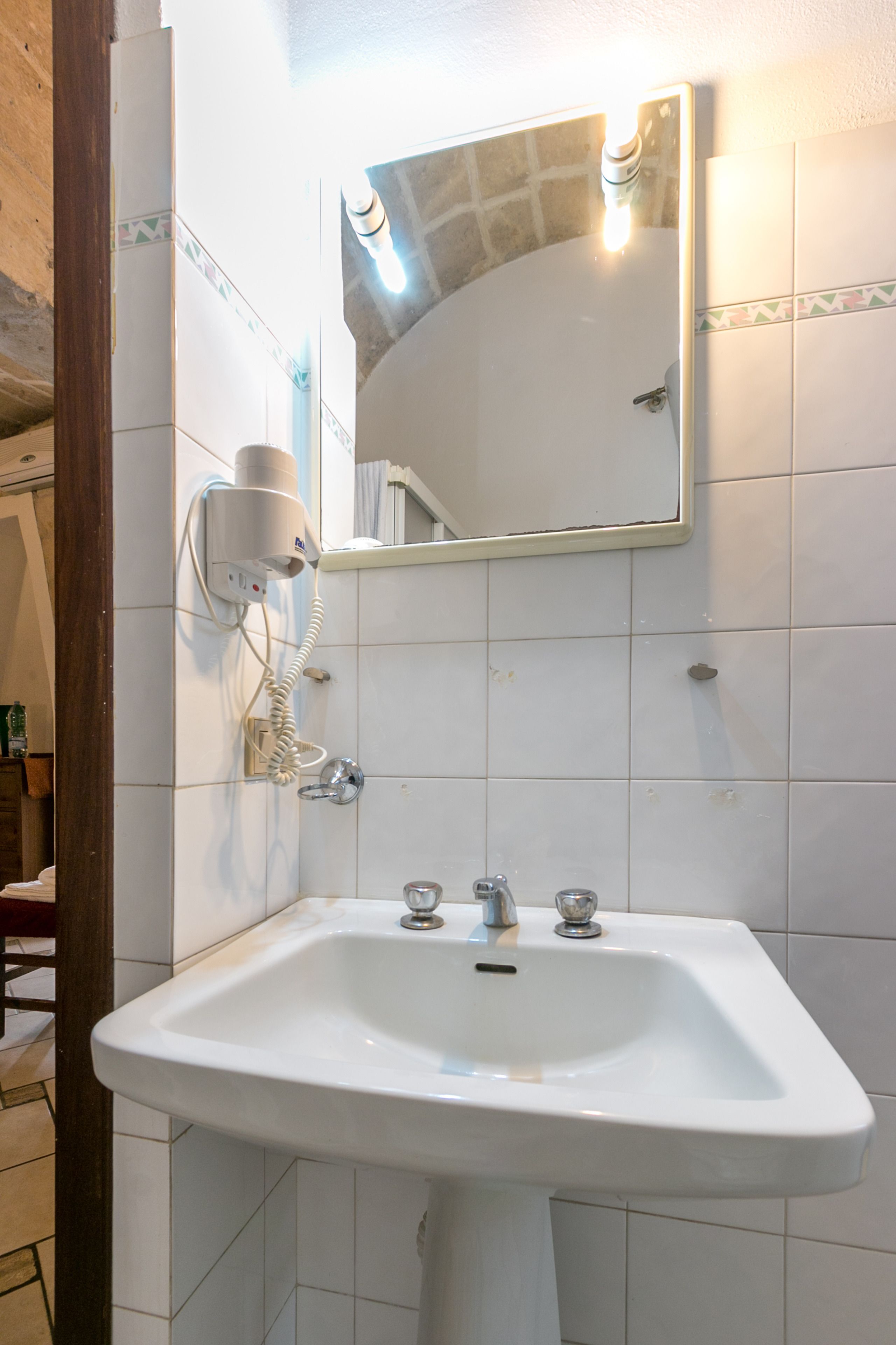 Casa de banho com uma pia branca, um espelho e um secador de cabelo fixado na parede.