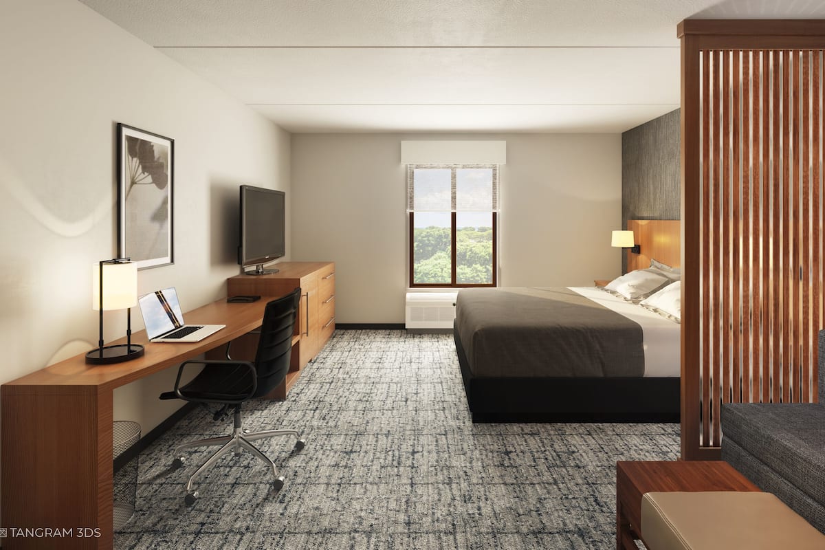 Quarto de hotel com cama, escrivaninha, cadeira, televisão e janela com vista para árvores.